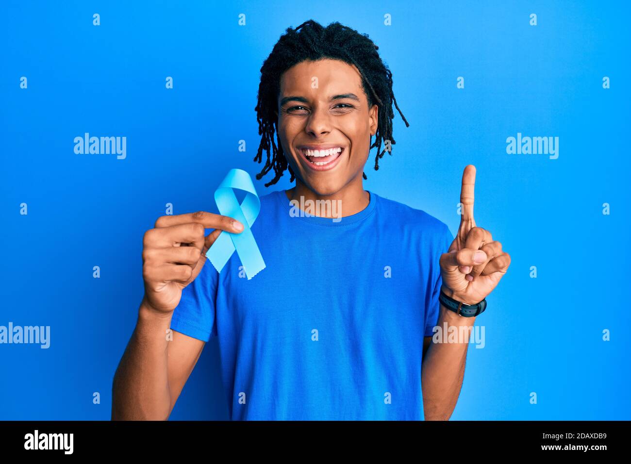 Young african american man holding blue ribbon smiling with an idea or ...