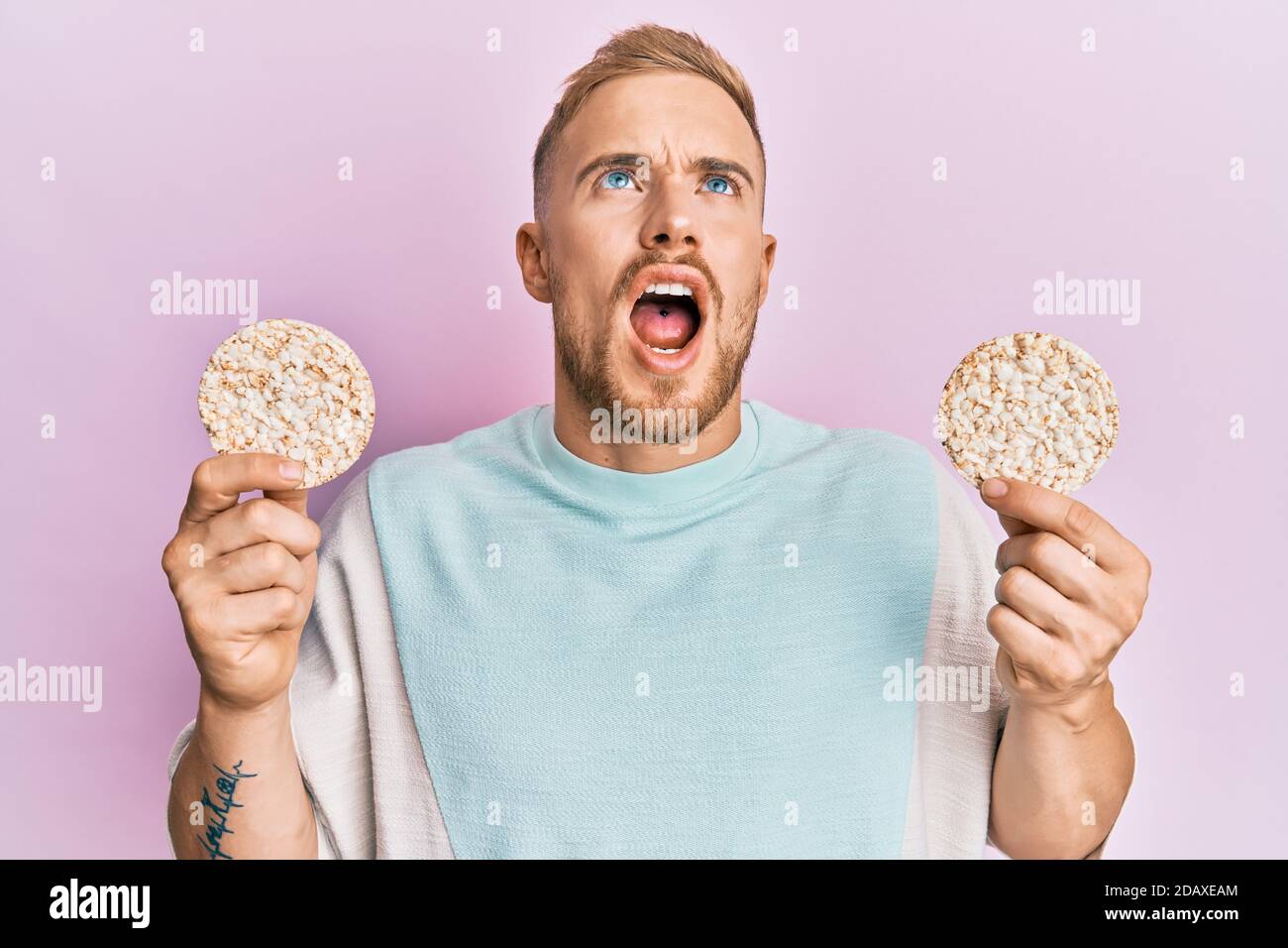 Young caucasian man eating healthy rice crackers angry and mad ...