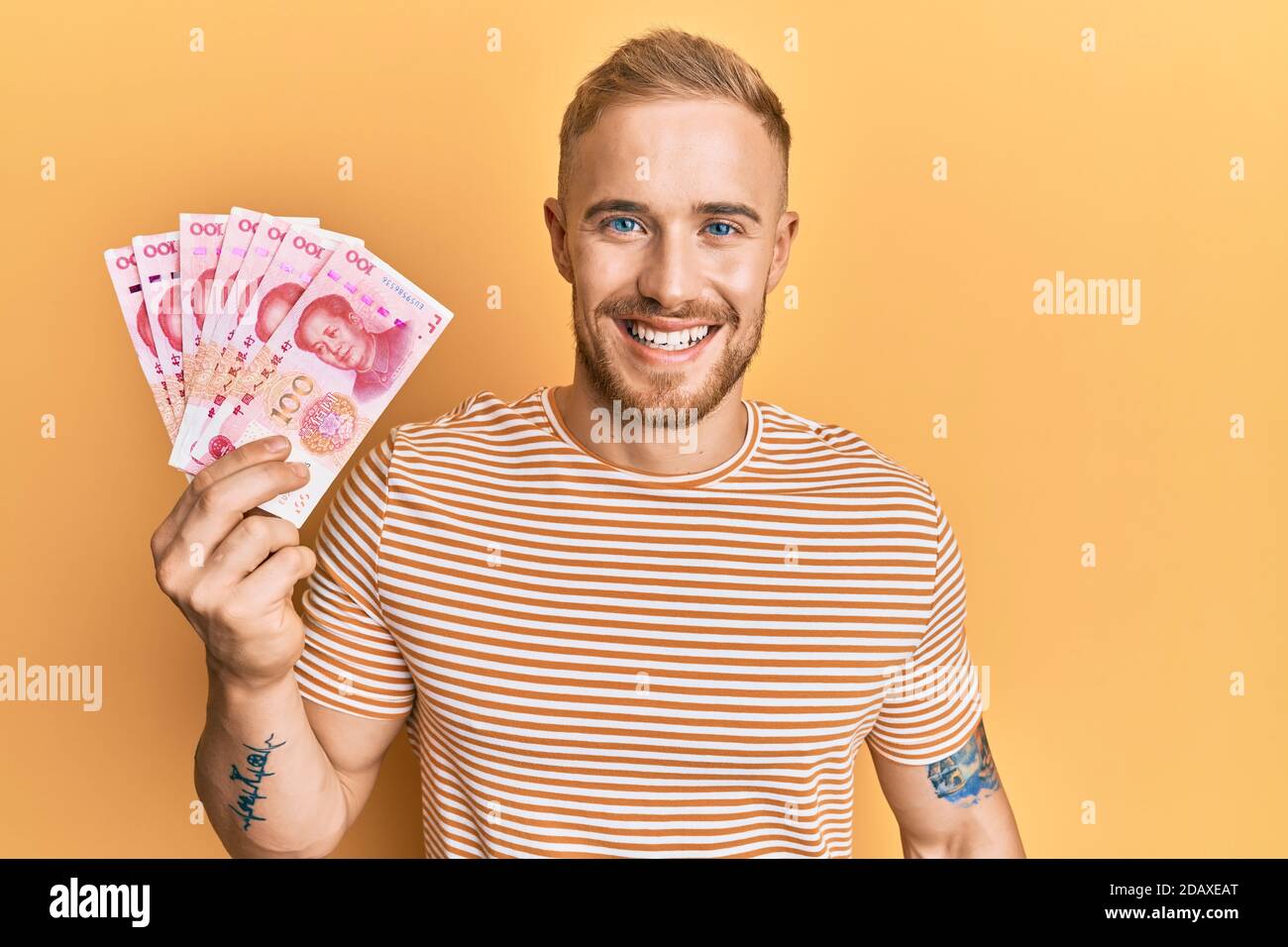 Young caucasian man holding 100 yuan chinese banknotes looking positive ...