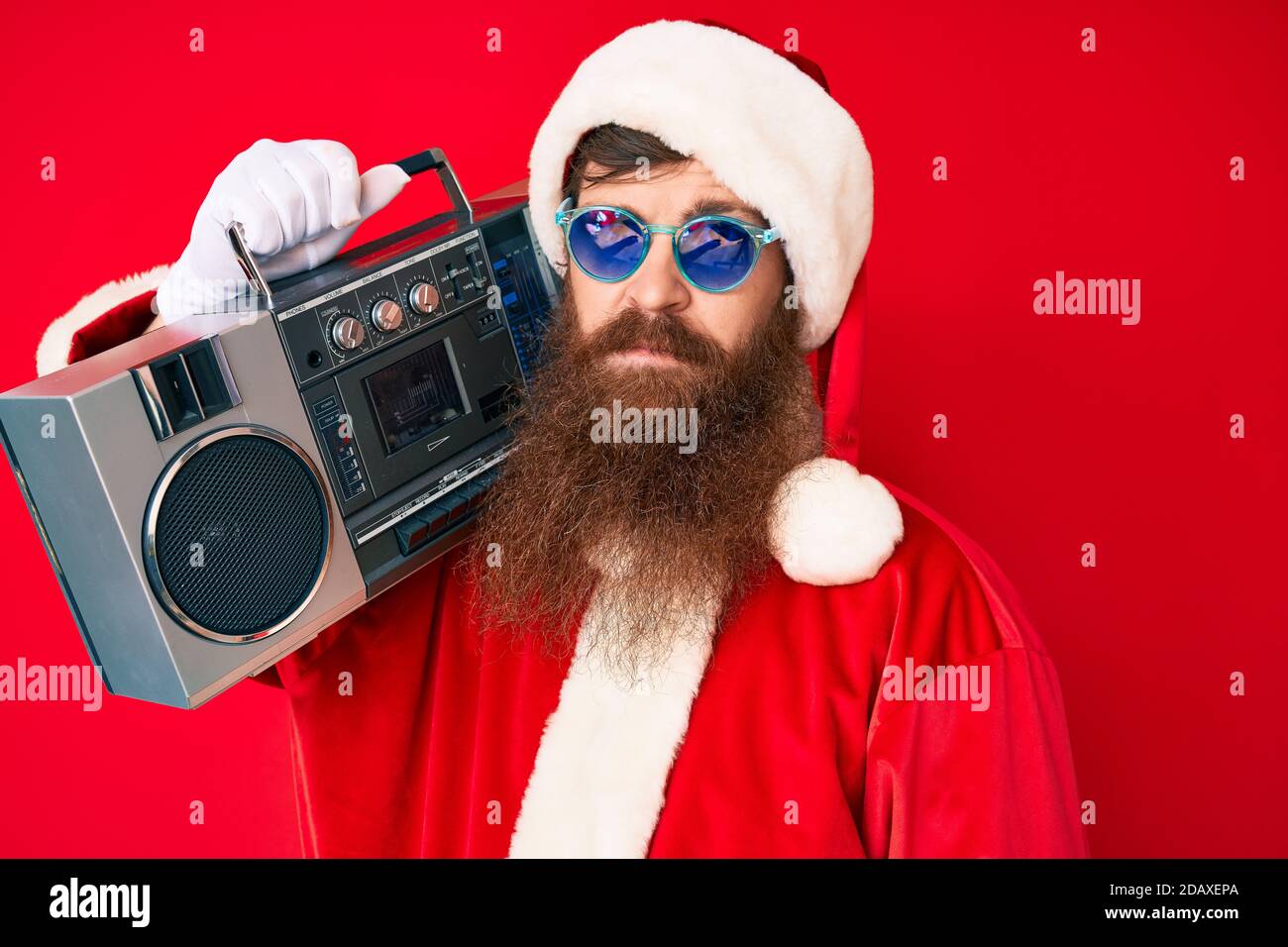 Handsome young red head man with long beard wearing santa claus costume ...