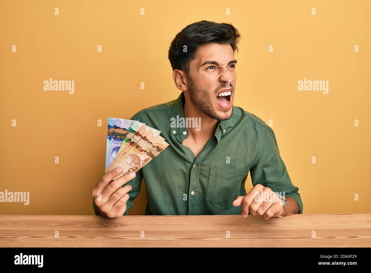 Young handsome man holding canadian dollars angry and mad screaming ...