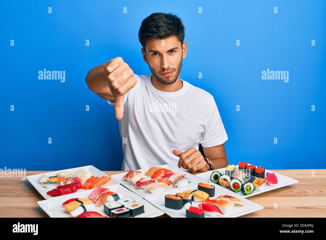 Young handsome man eating sushi sitting on the table looking unhappy ...