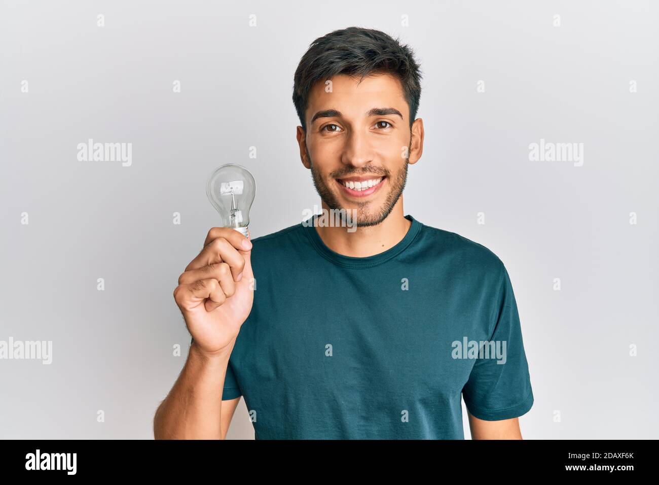 Young handsome man holding lightbulb for inspiration and idea looking ...