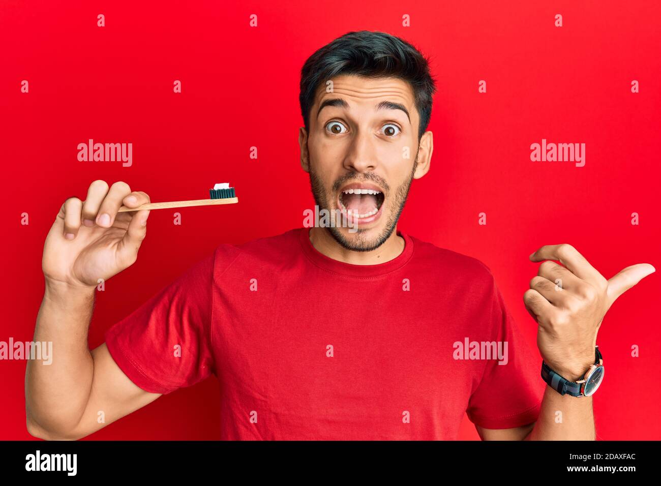 Young handsome man holding toothbrush with toothpaste pointing thumb up ...