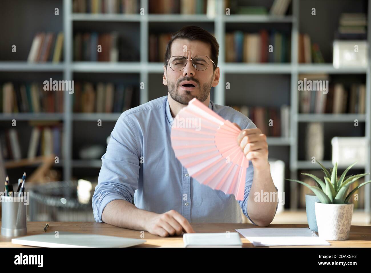 Man waving fan to reduce unbearable high temperature indoor Stock Photo ...