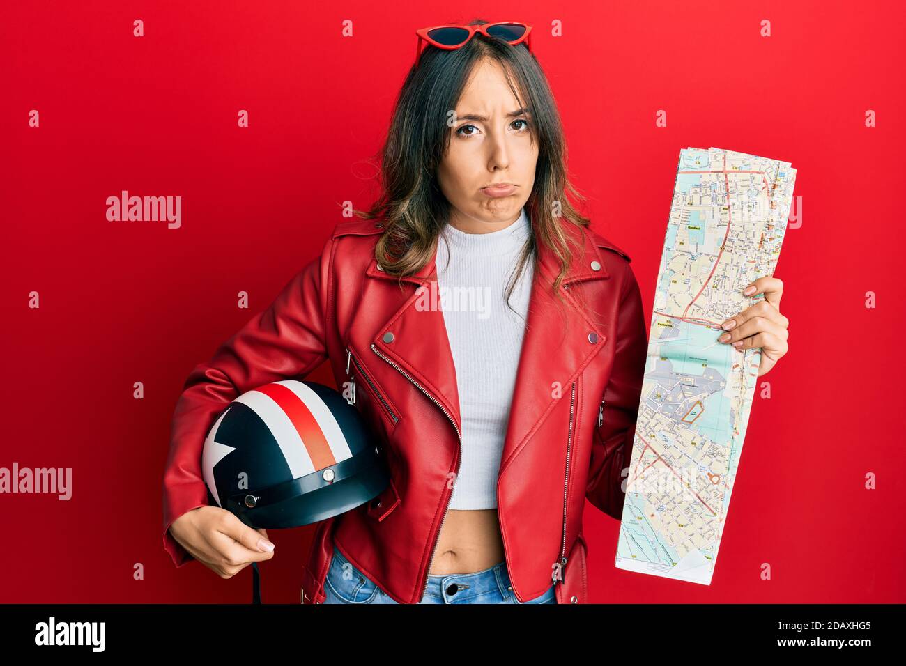 Young brunette woman holding motorbike helmet and city map puffing ...
