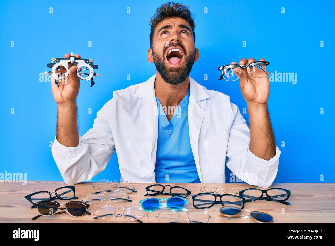 Young hispanic man with optometry glasses sitting at the table angry ...