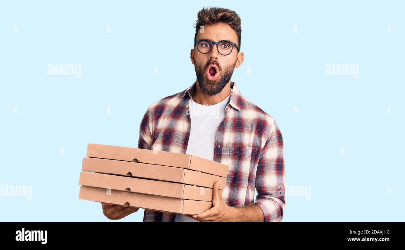 Young hispanic man holding delivery pizza box scared and amazed with ...