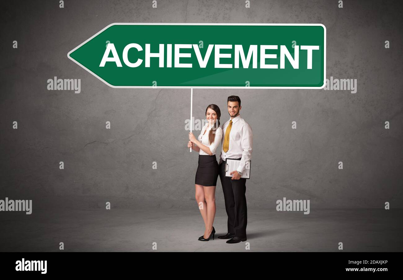 Young business person in casual holding road sign with ACHIEVEMENT ...