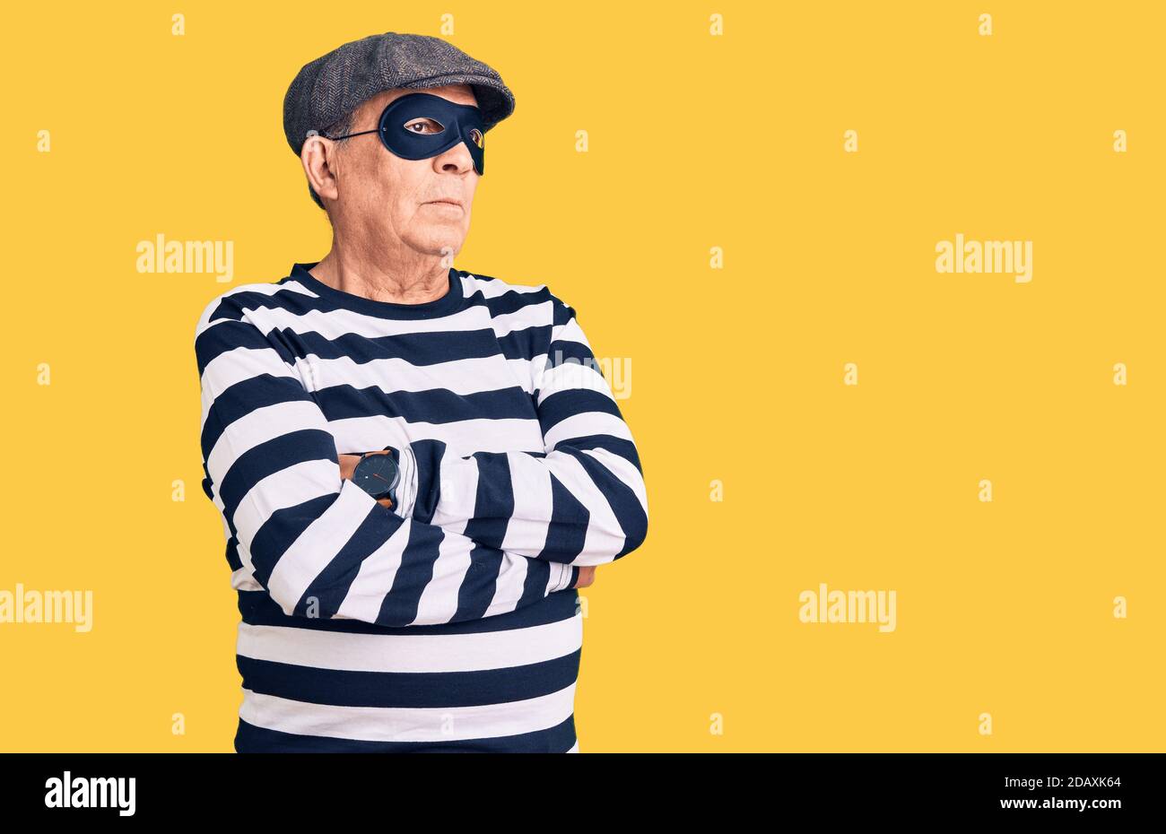 Senior handsome man wearing burglar mask and t-shirt looking to the ...