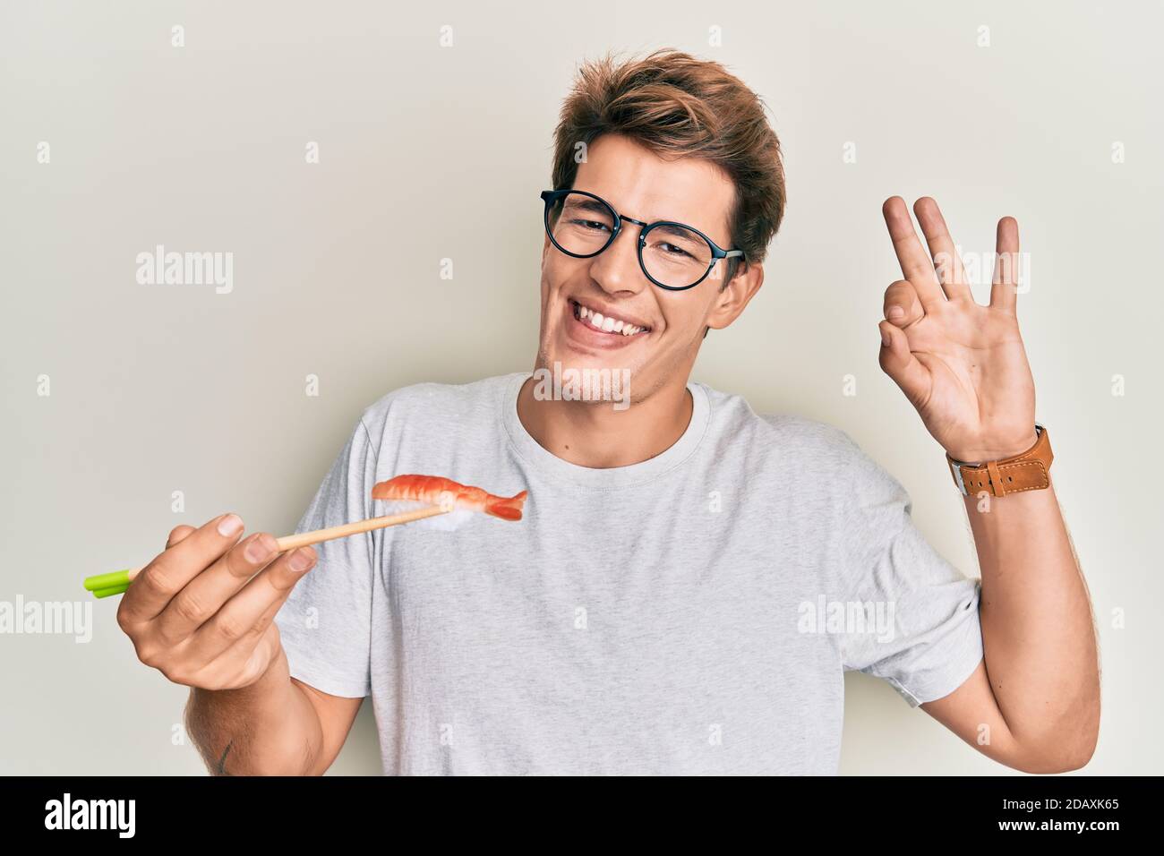 Handsome caucasian man eating prawn sushi using chopsticks doing ok ...
