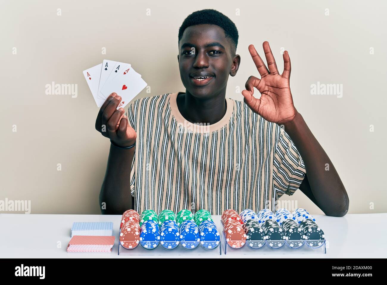 Young african american man playing poker holding cards doing ok sign ...