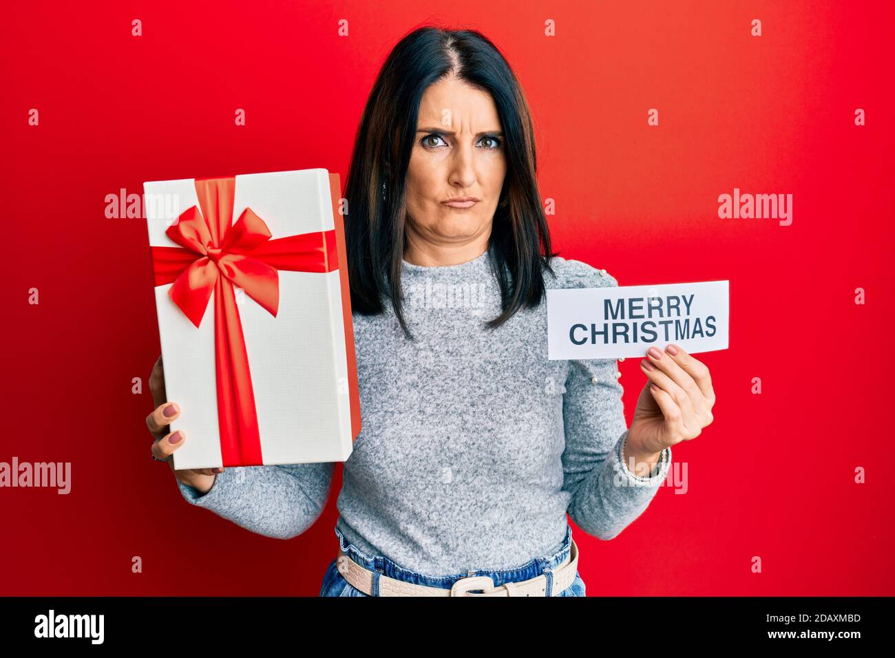 Middle age brunette woman holding merry christmas message and gift ...