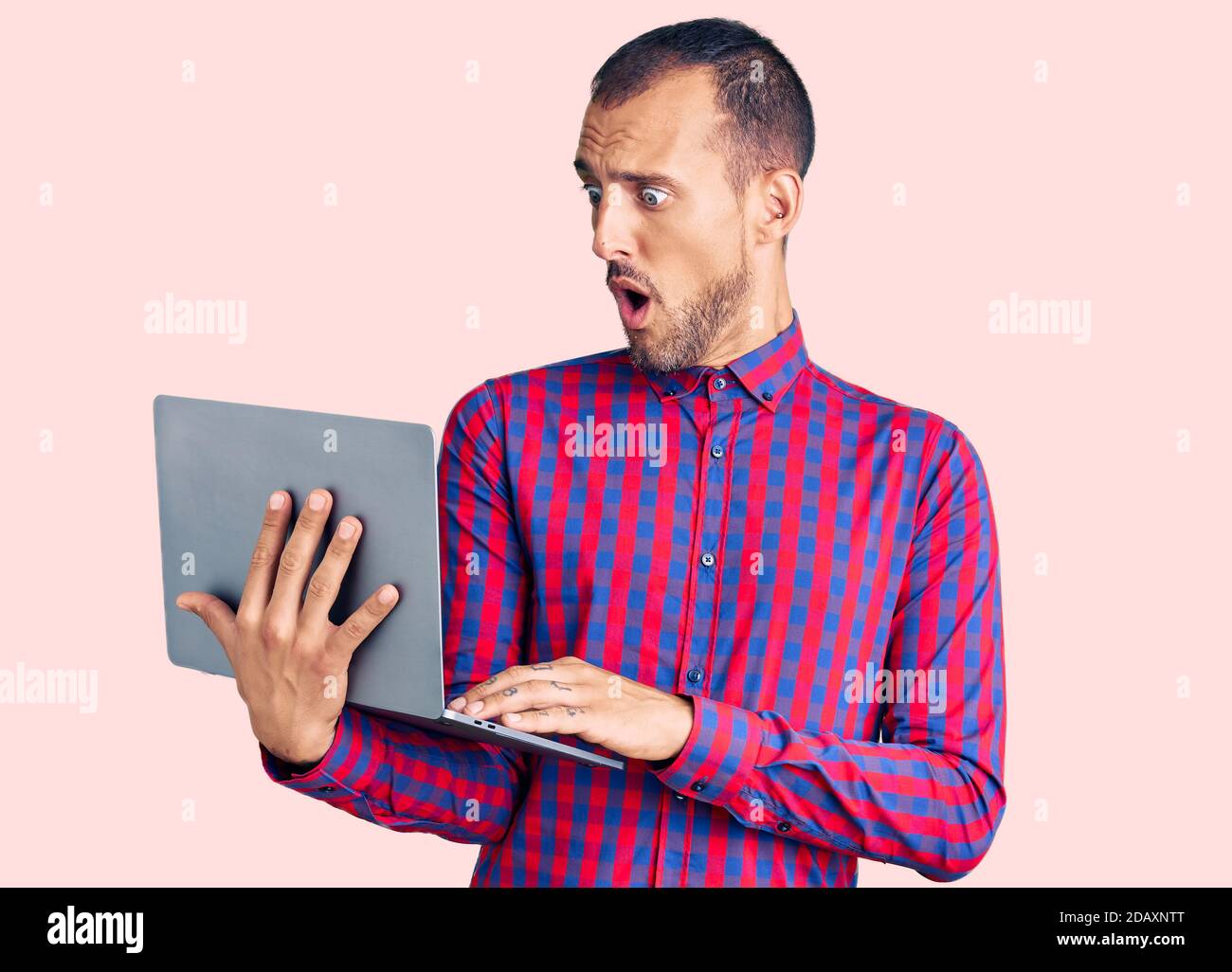 Young handsome man working using computer laptop scared and amazed with ...