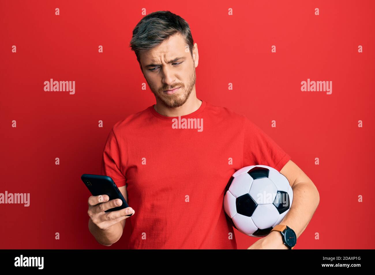 Handsome caucasian man holding football ball looking at smartphone in ...