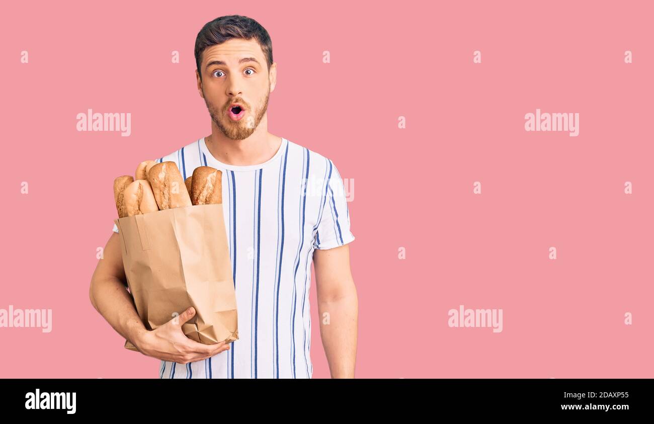 Handsome young man with bear holding paper bag with bread scared and ...