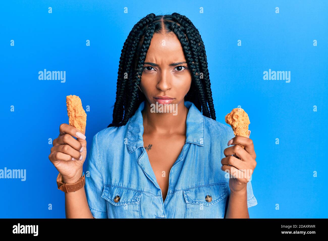 Beautiful hispanic woman eating chicken wings skeptic and nervous ...