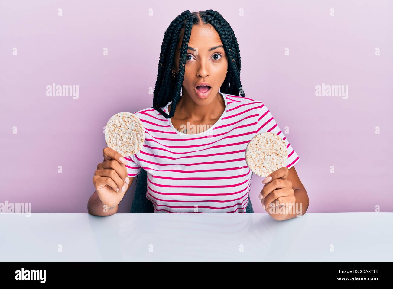 Beautiful hispanic woman eating healthy rice crackers afraid and ...