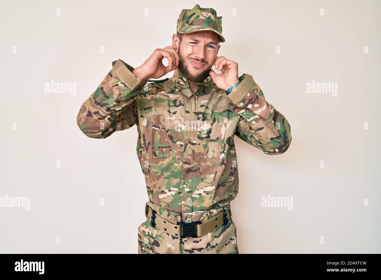 Young caucasian man wearing camouflage army uniform covering ears with ...