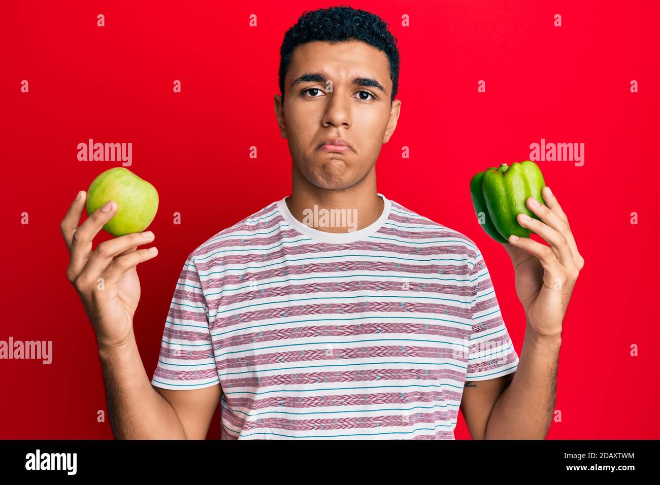 Young arab man holding green apple and pepper depressed and worry for ...
