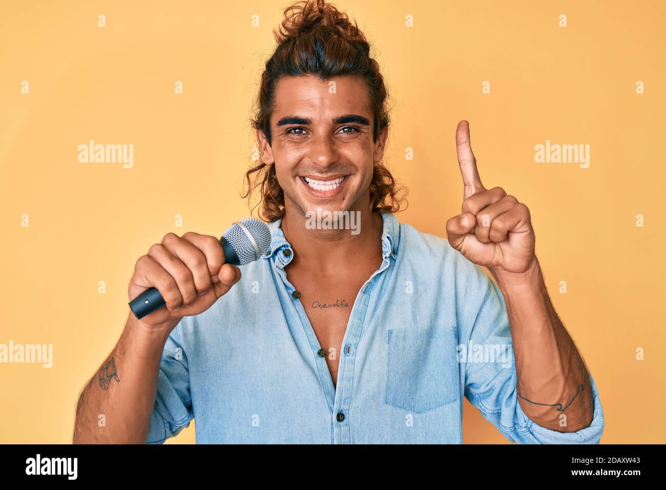 Young hispanic man singing song using microphone smiling with an idea ...