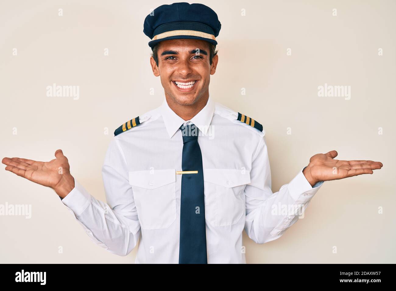 Young hispanic man wearing airplane pilot uniform smiling showing both ...