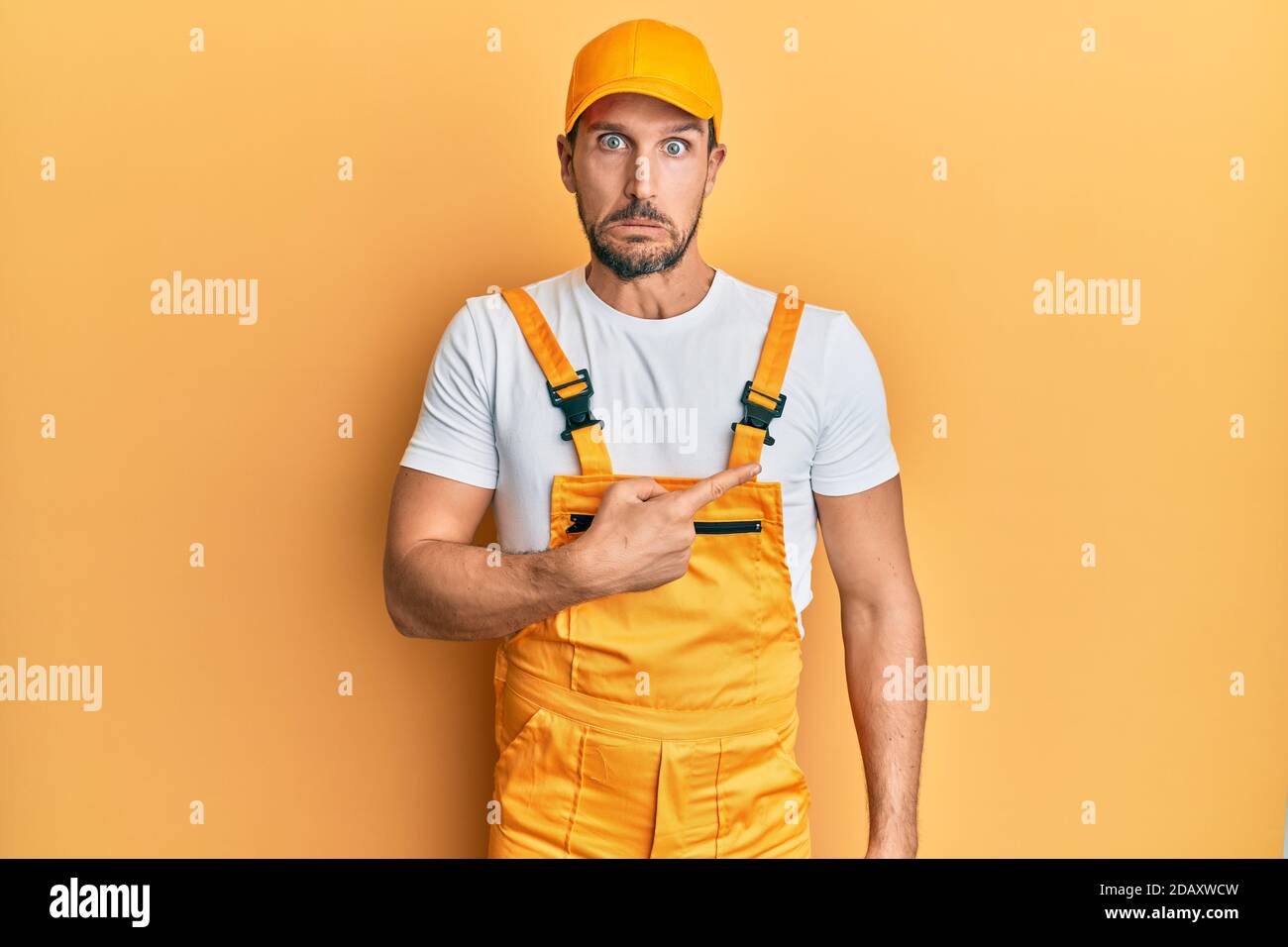 Young handsome man wearing handyman uniform over yellow background ...