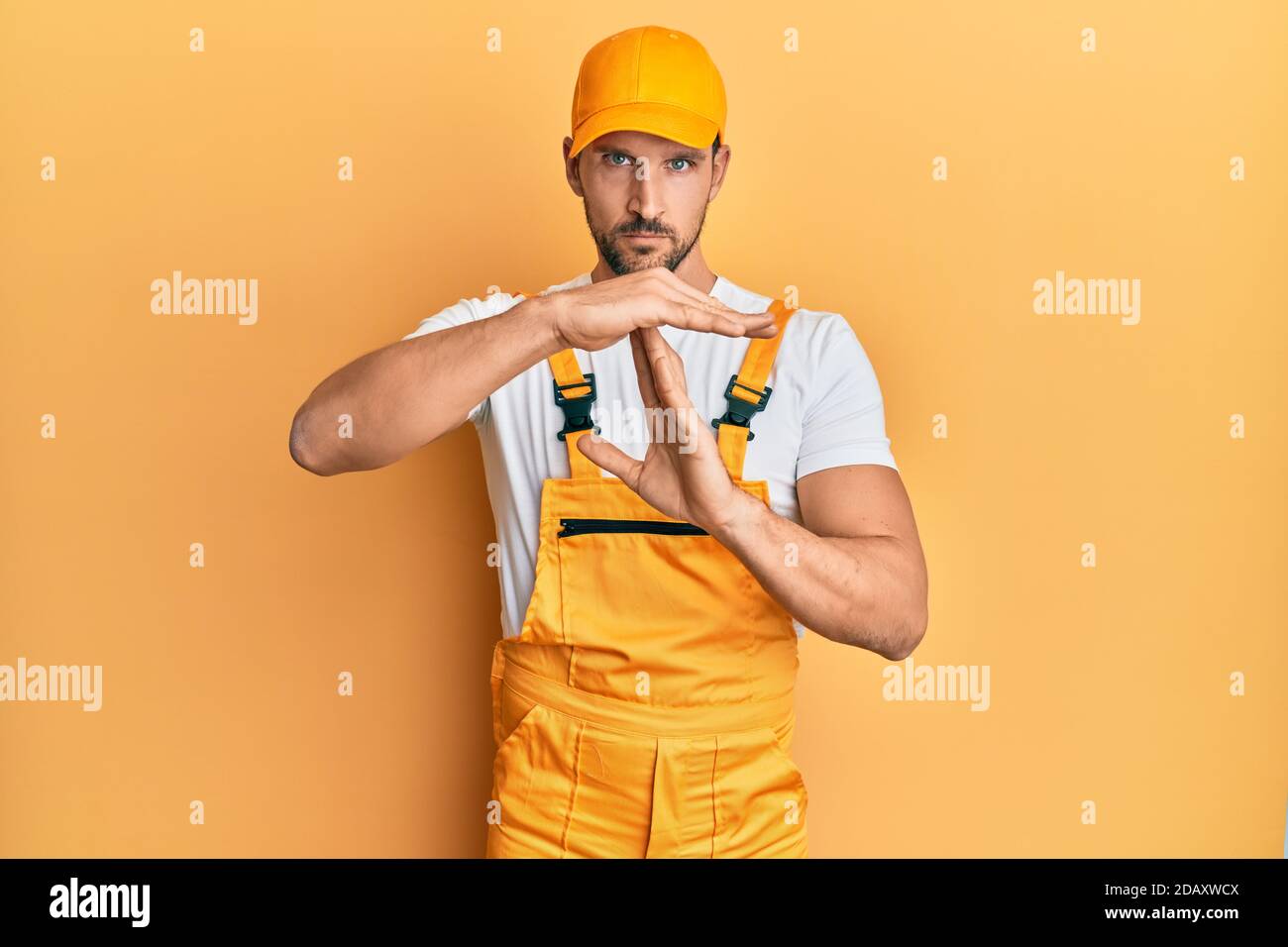Young handsome man wearing handyman uniform over yellow background ...