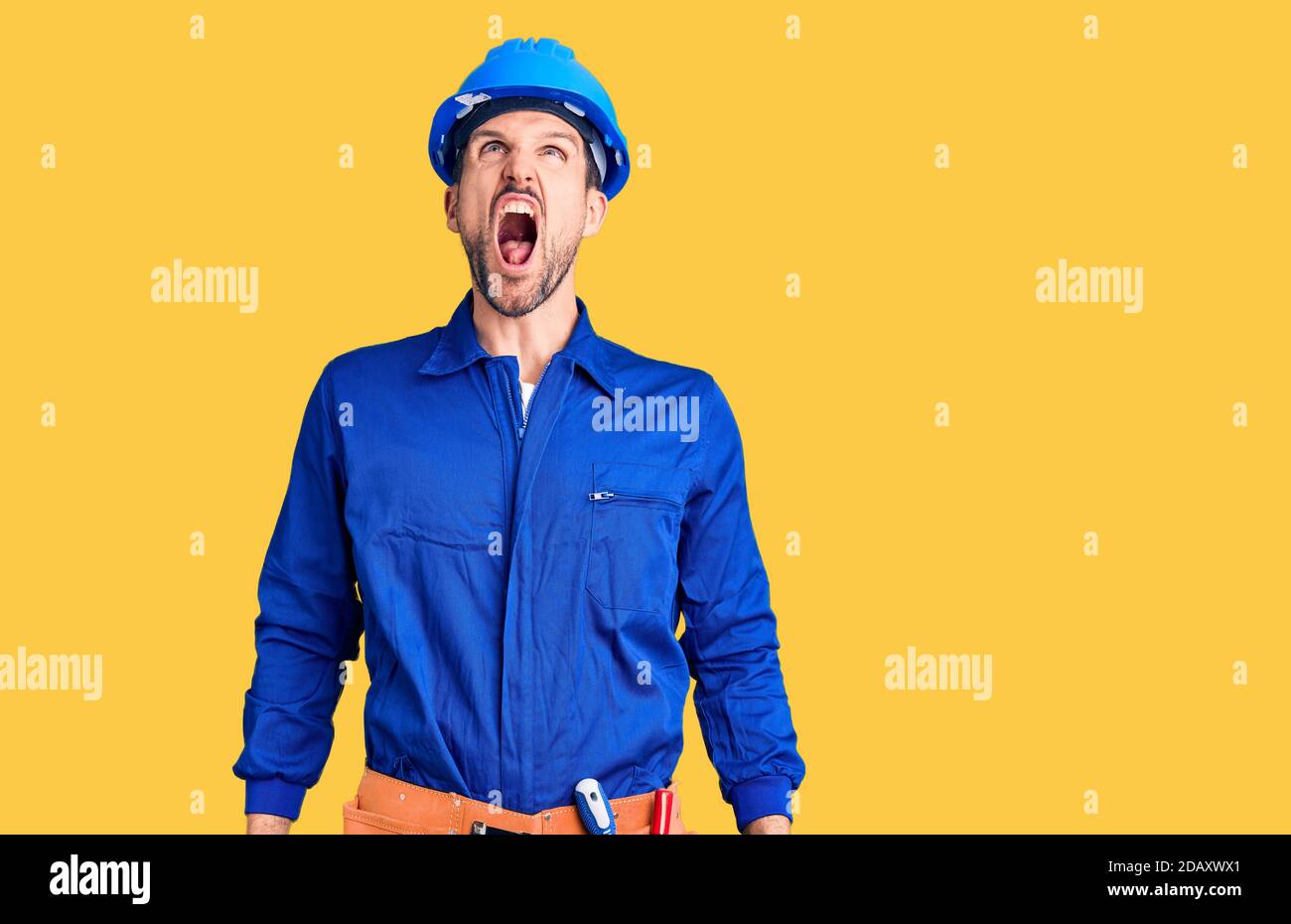 Young handsome man wearing worker uniform and hardhat angry and mad ...