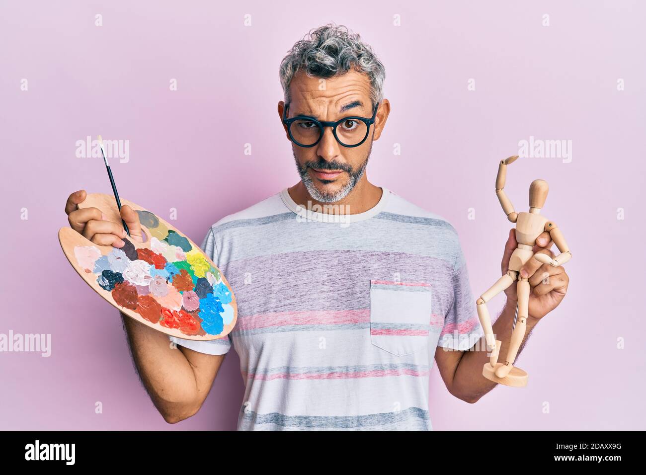Middle age grey-haired man holding palette and manikin skeptic and ...