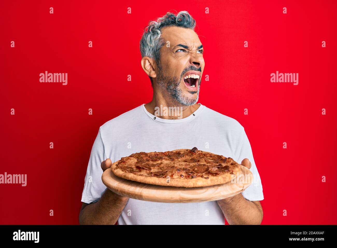 Middle age grey-haired man holding italian pizza angry and mad ...