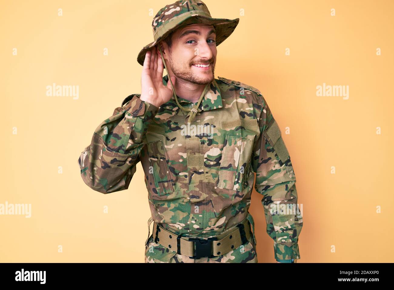 Young caucasian man wearing camouflage army uniform smiling with hand over ear listening an ...