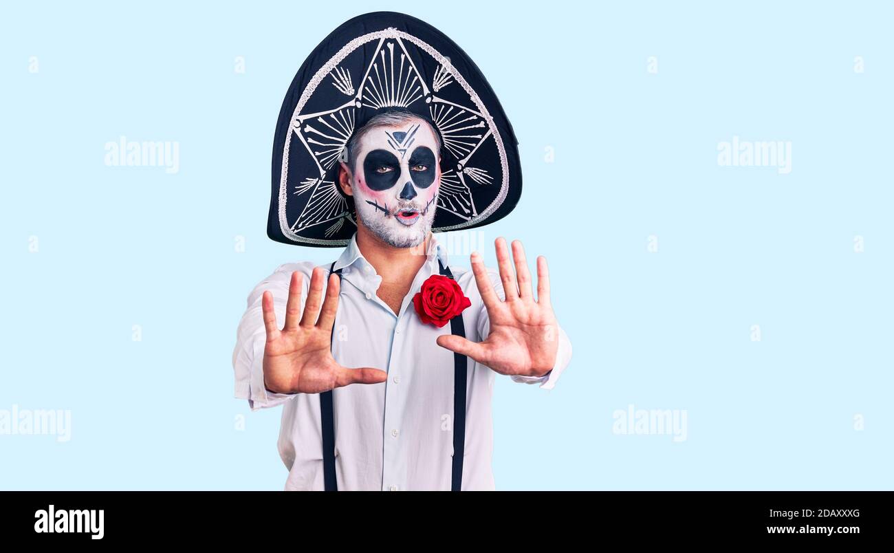 Man wearing day of the dead costume over background doing stop gesture ...