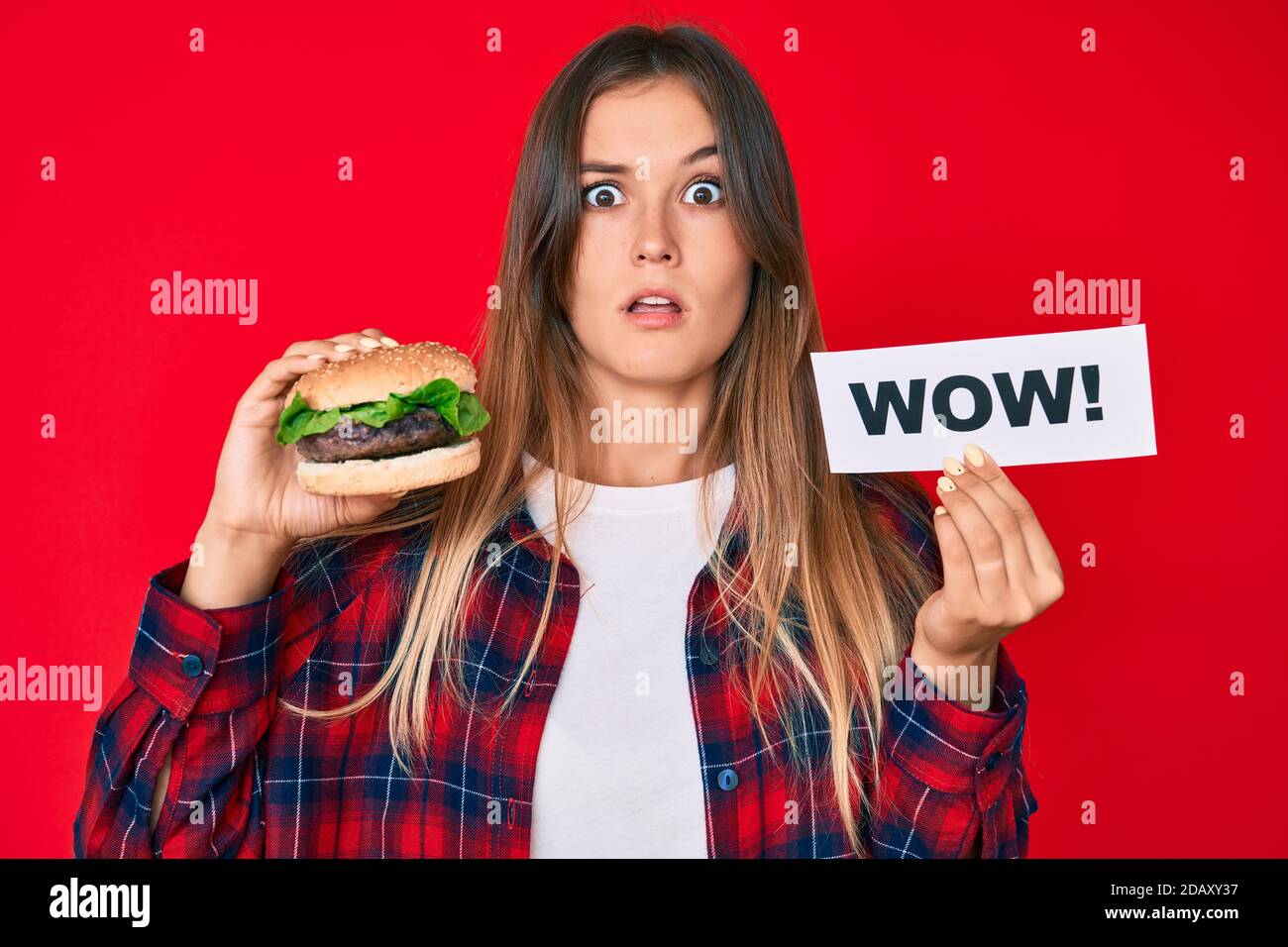 Beautiful caucasian woman eating a tasty classic burger holding wow ...