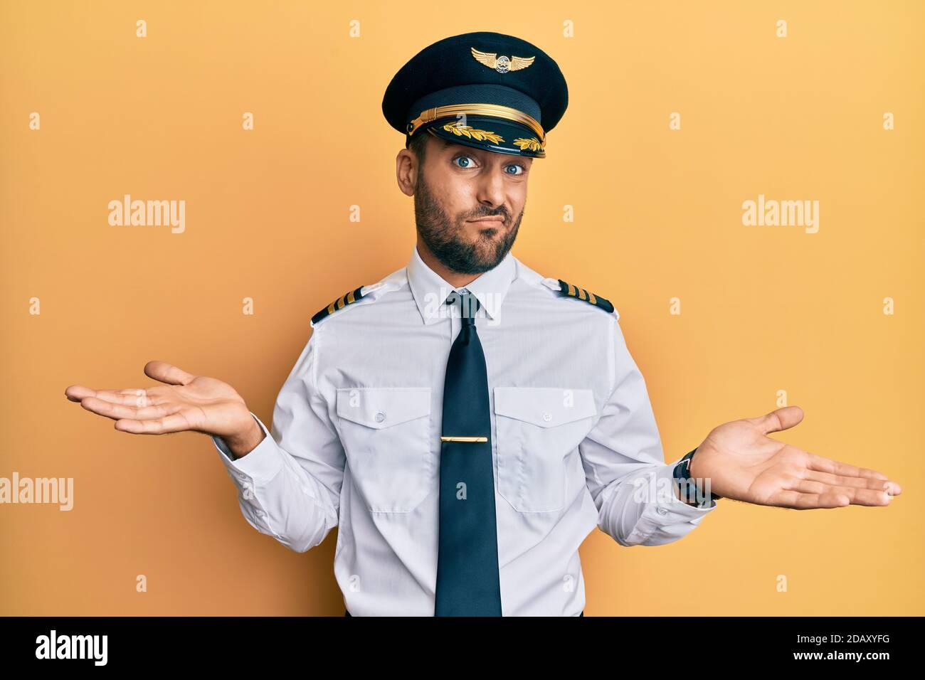Handsome hispanic man wearing airplane pilot uniform clueless and ...