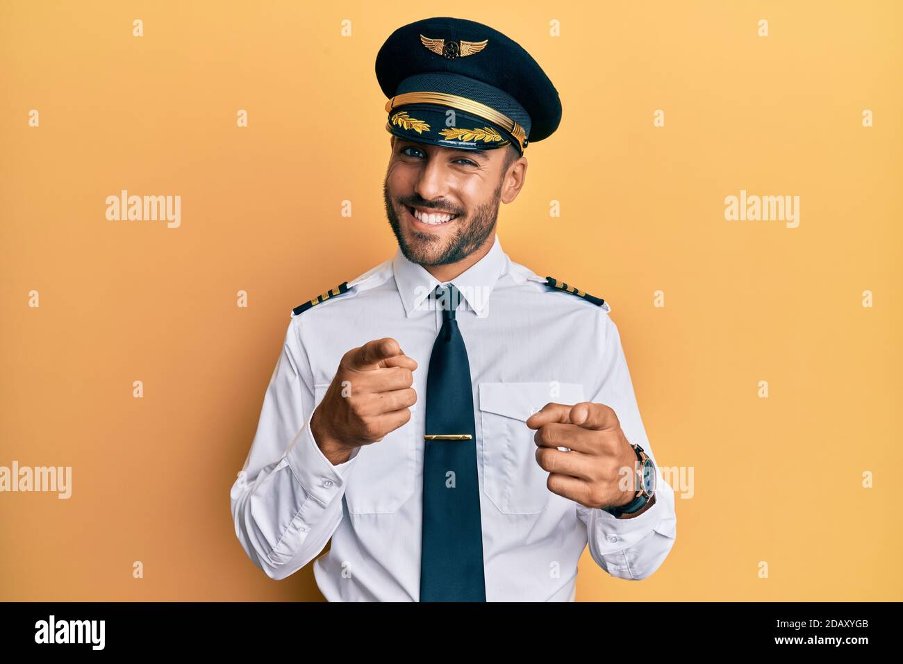 Handsome hispanic man wearing airplane pilot uniform pointing fingers ...