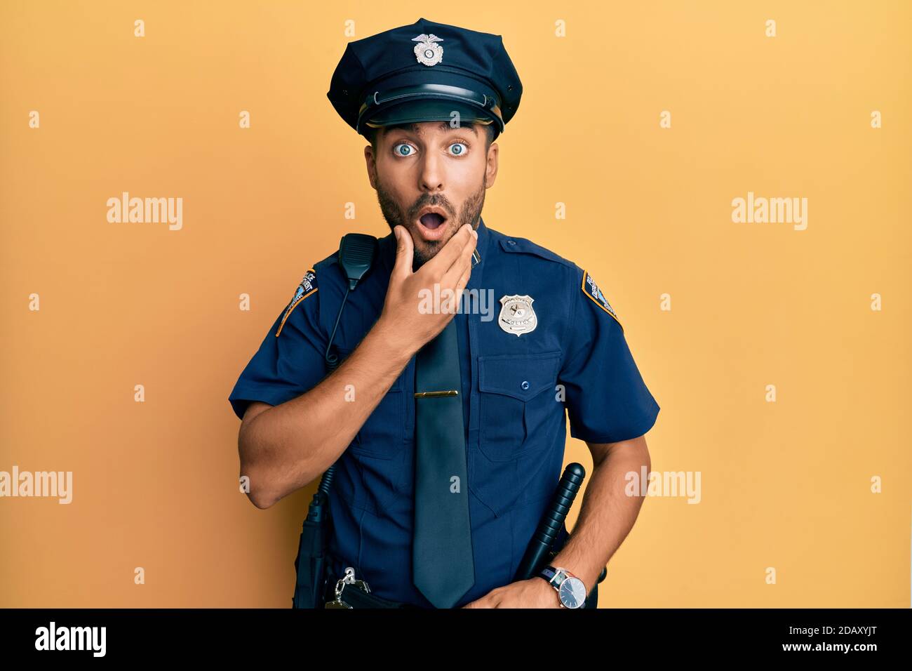 Handsome hispanic man wearing police uniform looking fascinated with ...