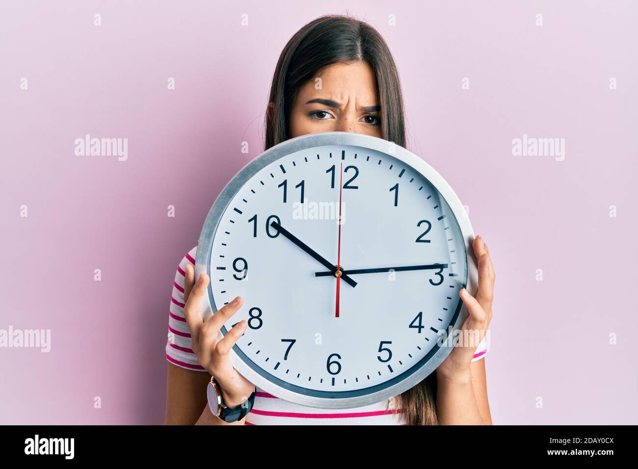 Young brunette woman holding big clock covering face depressed and ...
