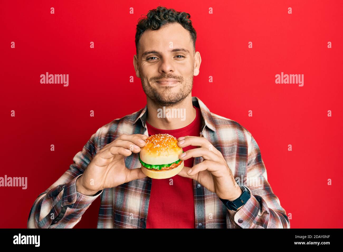 Handsome man with beard eating hamburger making fish face with mouth ...