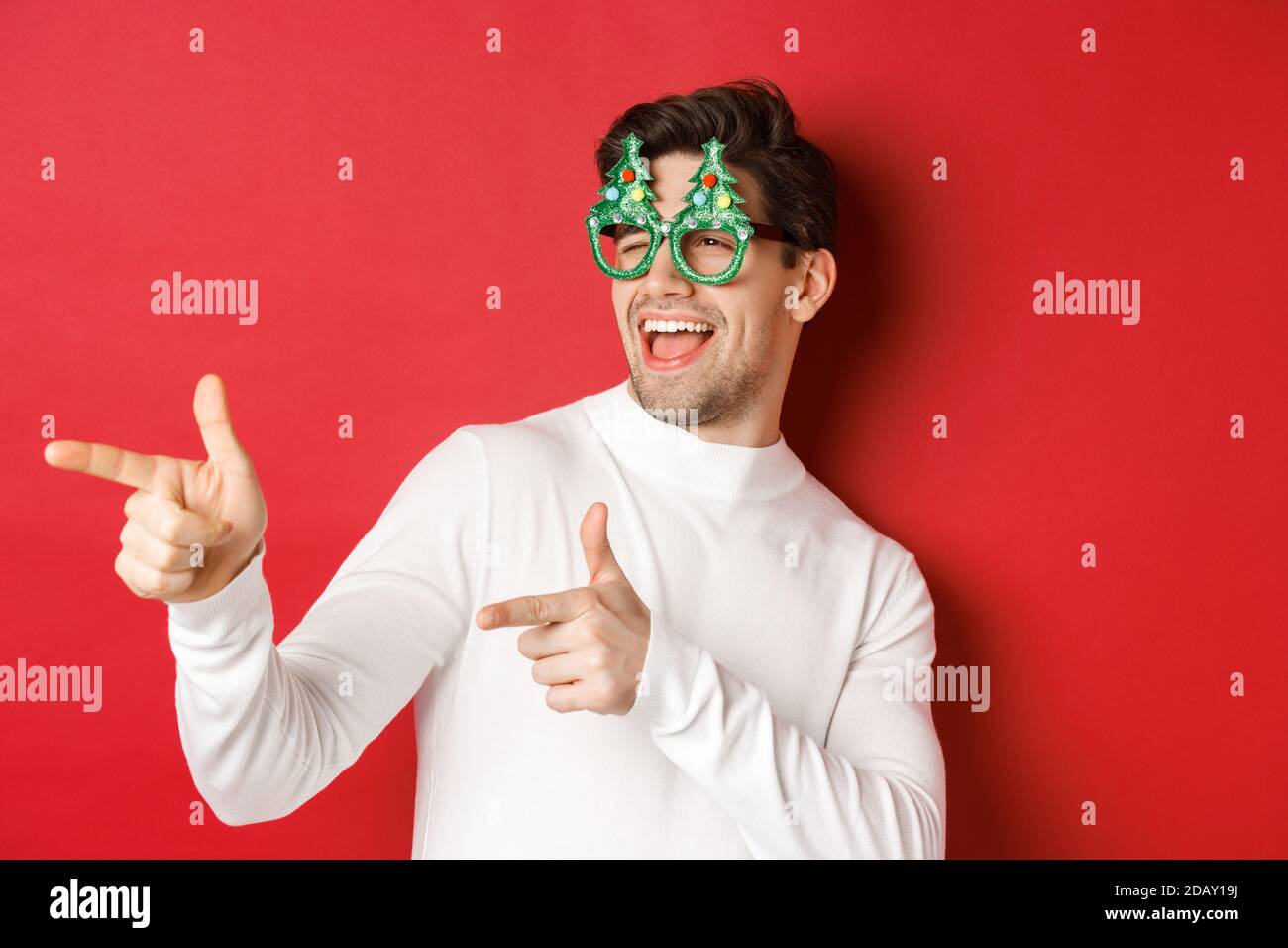 Close-up of cheeky handsome man in party glasses, pointing finger left ...