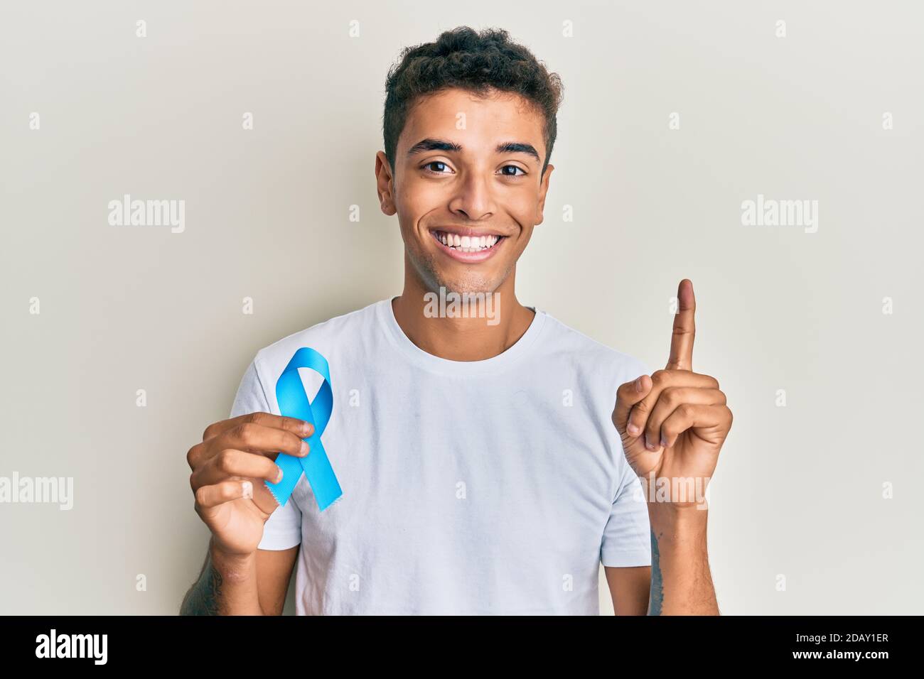 Young handsome african american man holding blue ribbon smiling with an ...