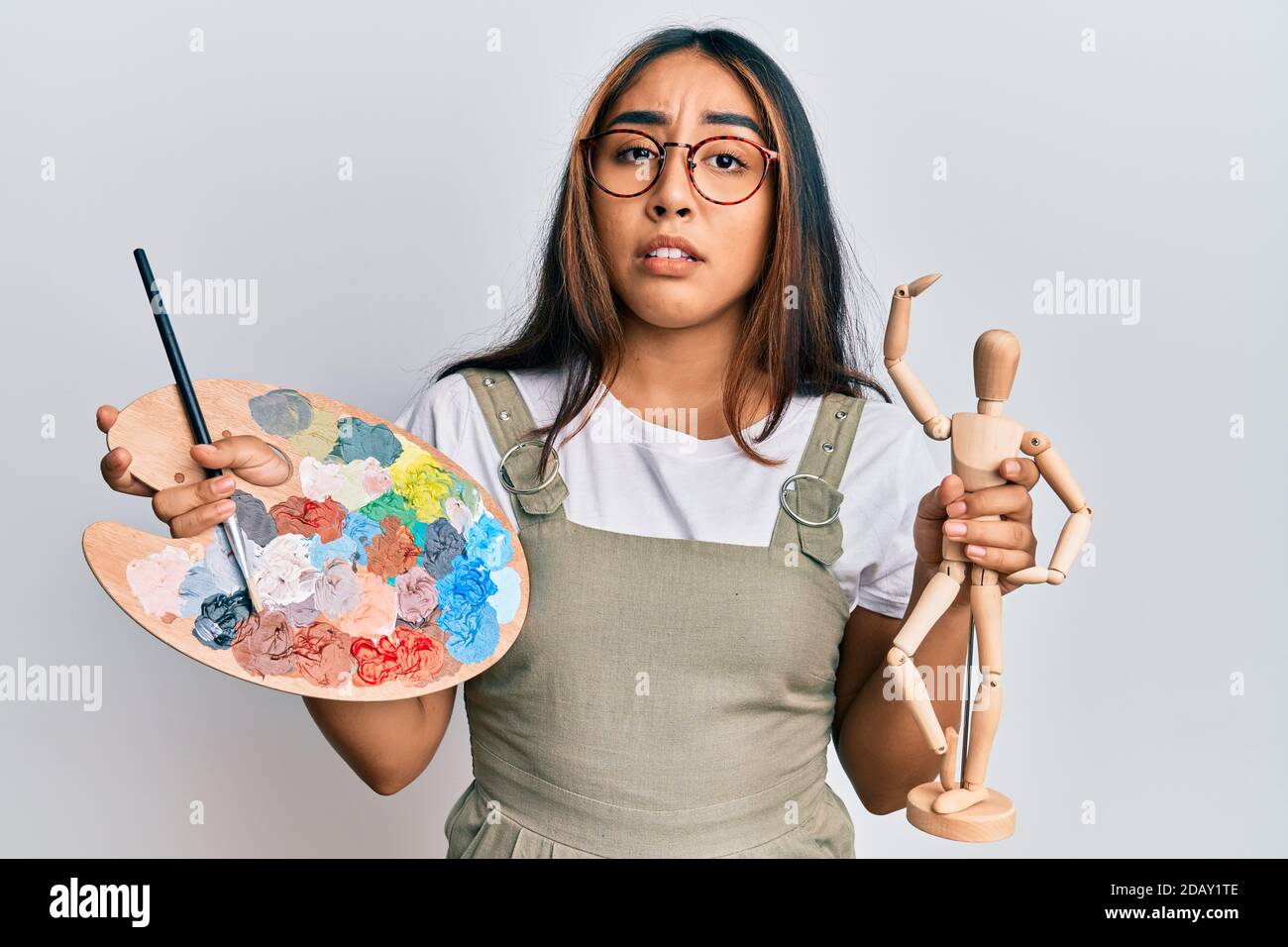 Young latin woman artist holding palette and manikin clueless and ...