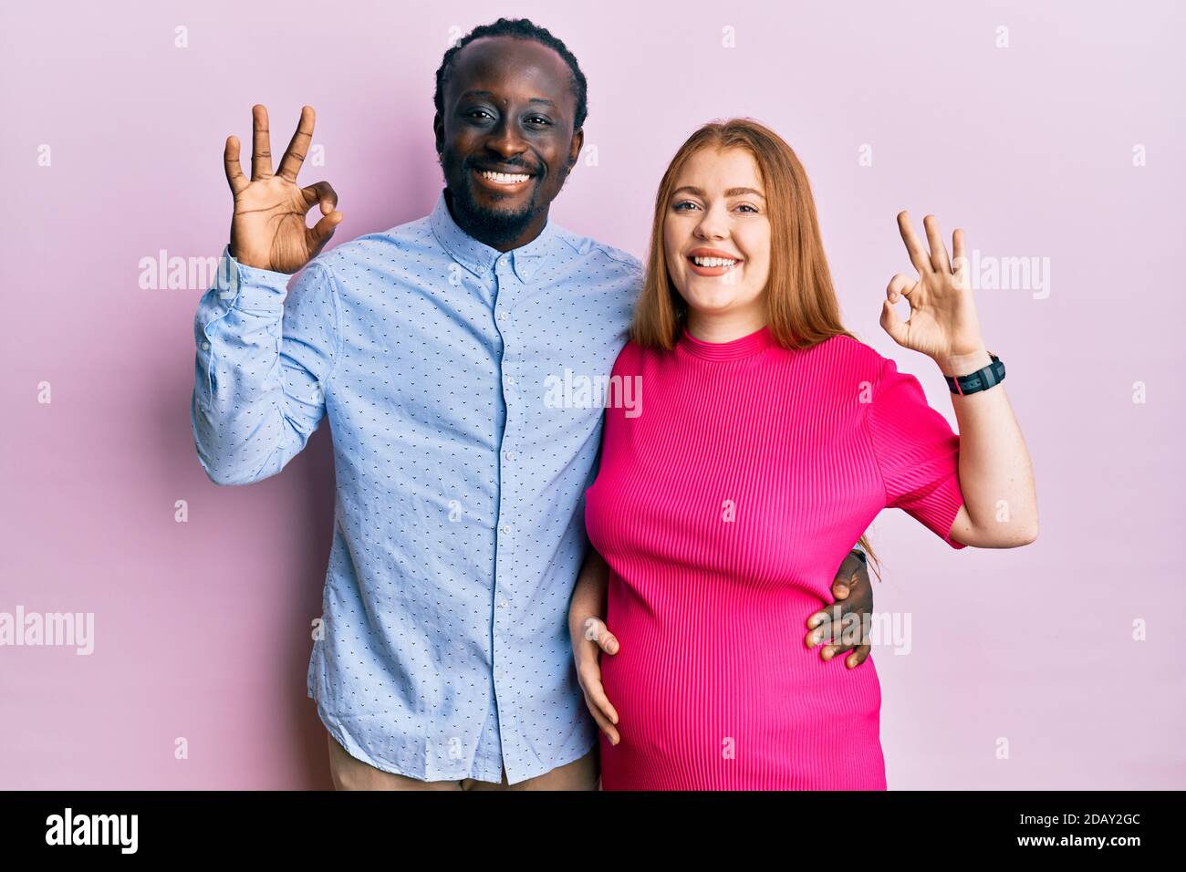 Young interracial couple expecting a baby, touching pregnant belly ...
