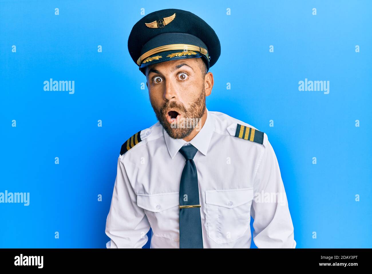 Handsome man with beard wearing airplane pilot uniform afraid and ...