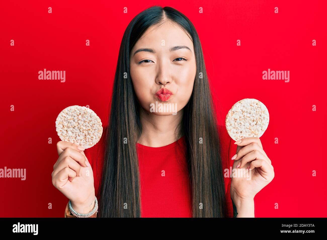 Young chinese woman eating healthy rice crackers puffing cheeks with ...