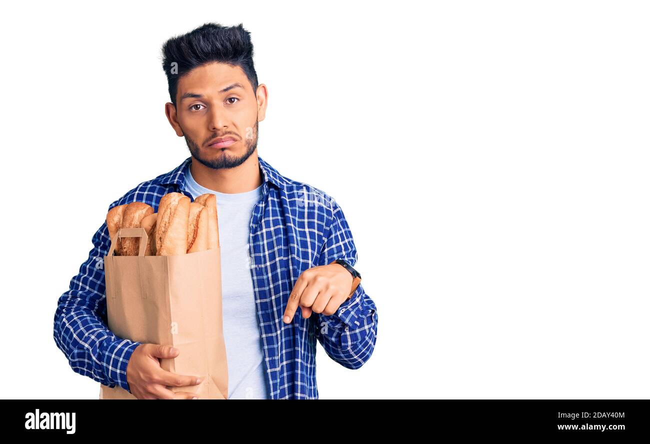 Handsome latin american young man holding paper bag with bread pointing ...