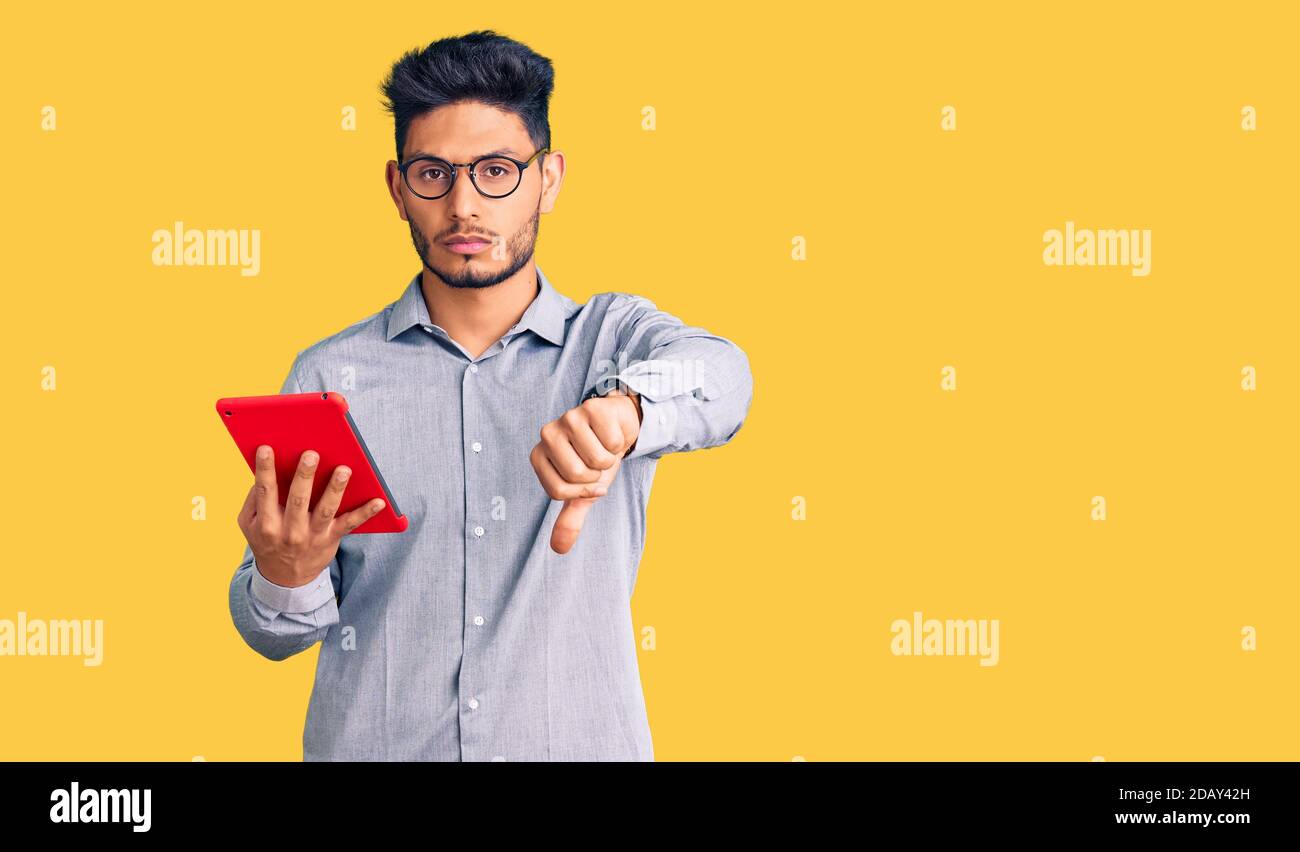 Handsome latin american young man holding touchpad with angry face ...