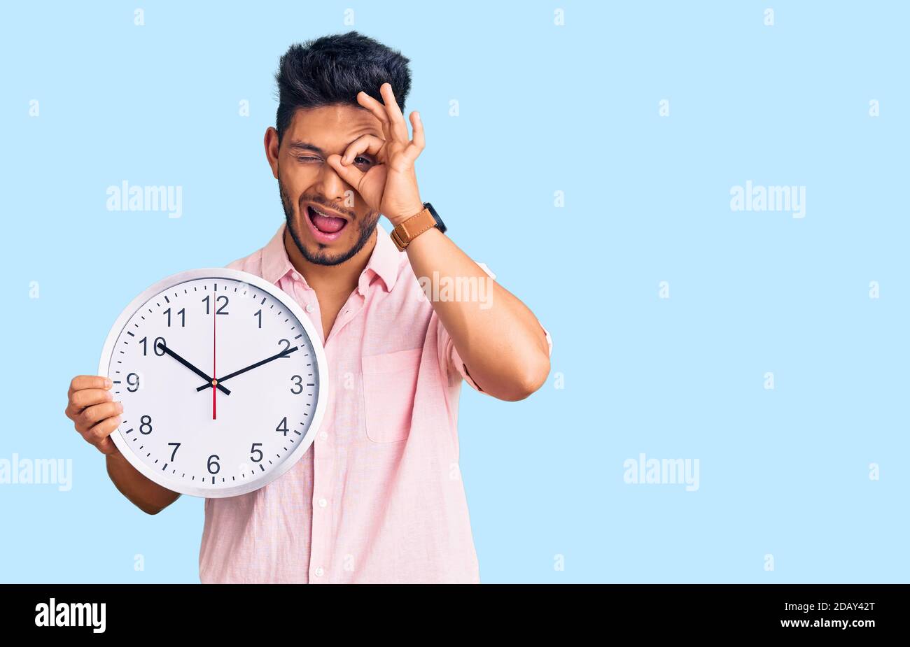 Handsome latin american young man holding big clock smiling happy doing ...