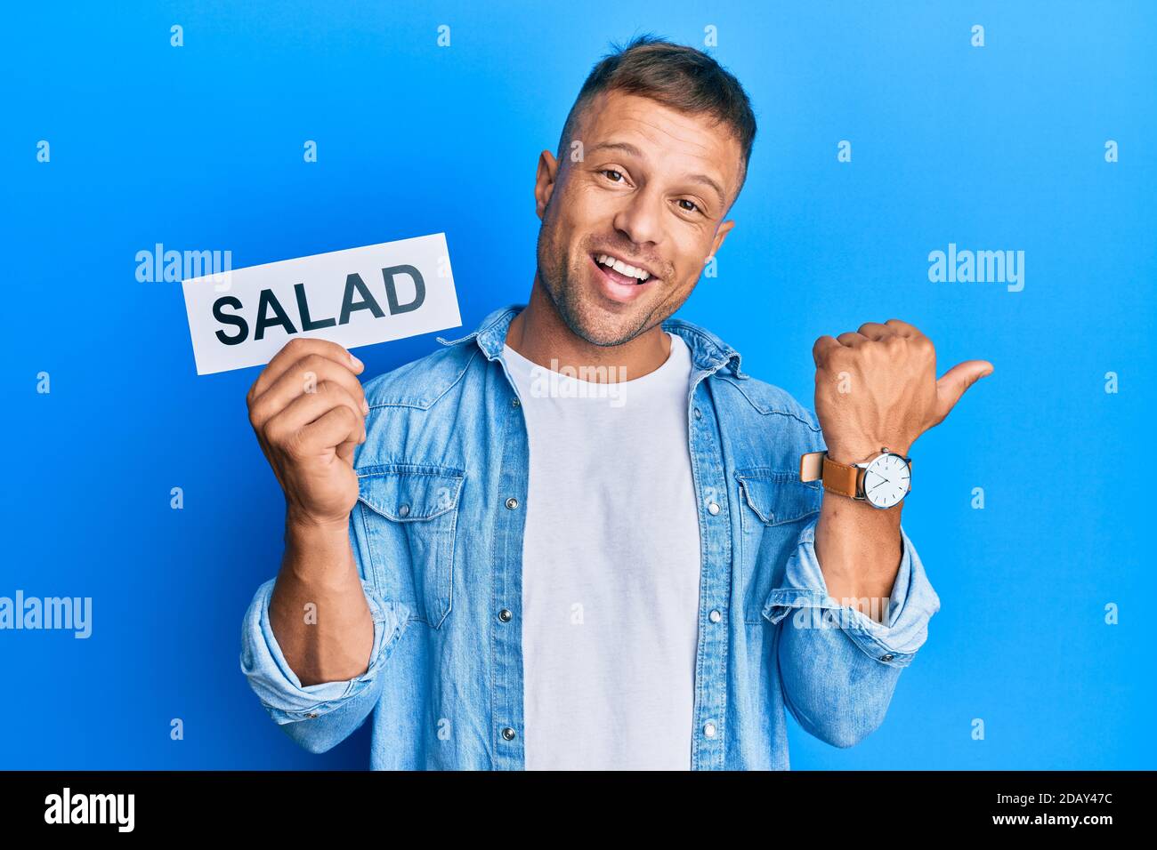 Handsome muscle man holding salad word on paper pointing thumb up to ...