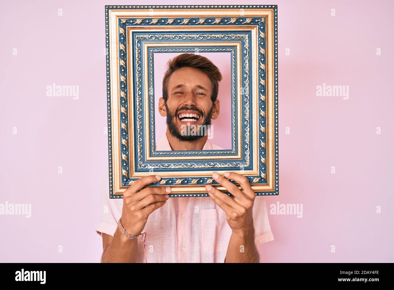 Handsome caucasian man with beard holding empty frame smiling and ...